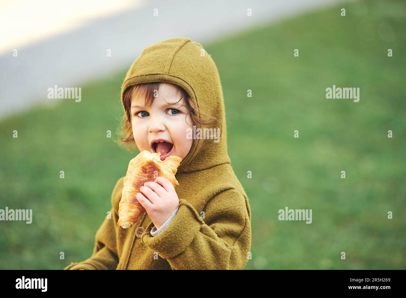 Outdoor portrait of cute 1 - 2 year old toddler kid eating croissant ...