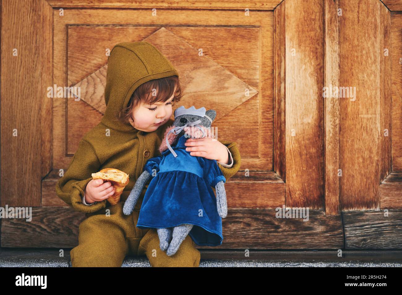 Outdoor portrait of adorable toddler girl eating croissant, playing ...