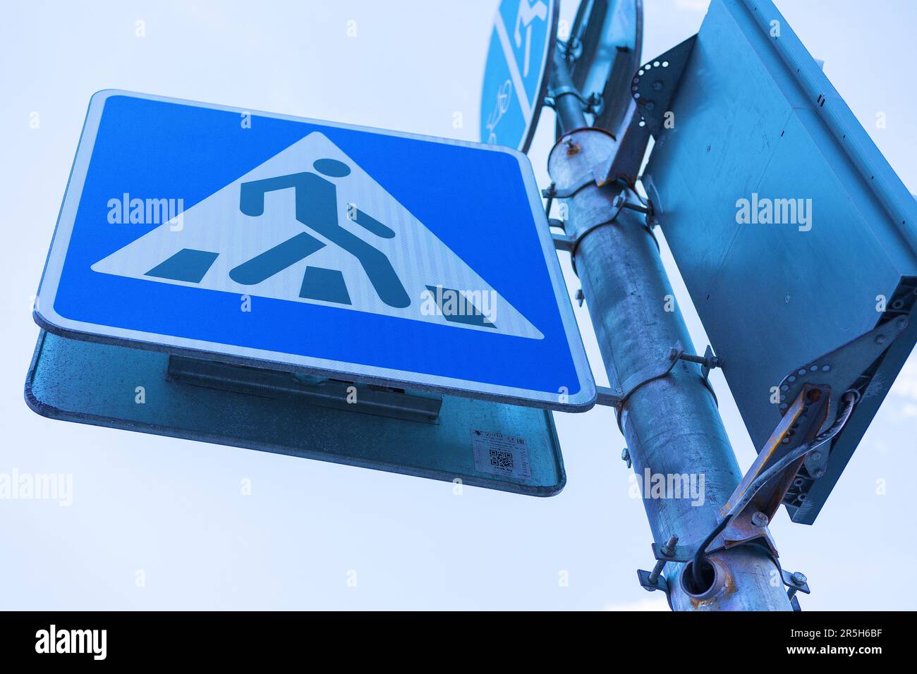 A pedestrian crossing sign on a gray metal pole with a partially ...