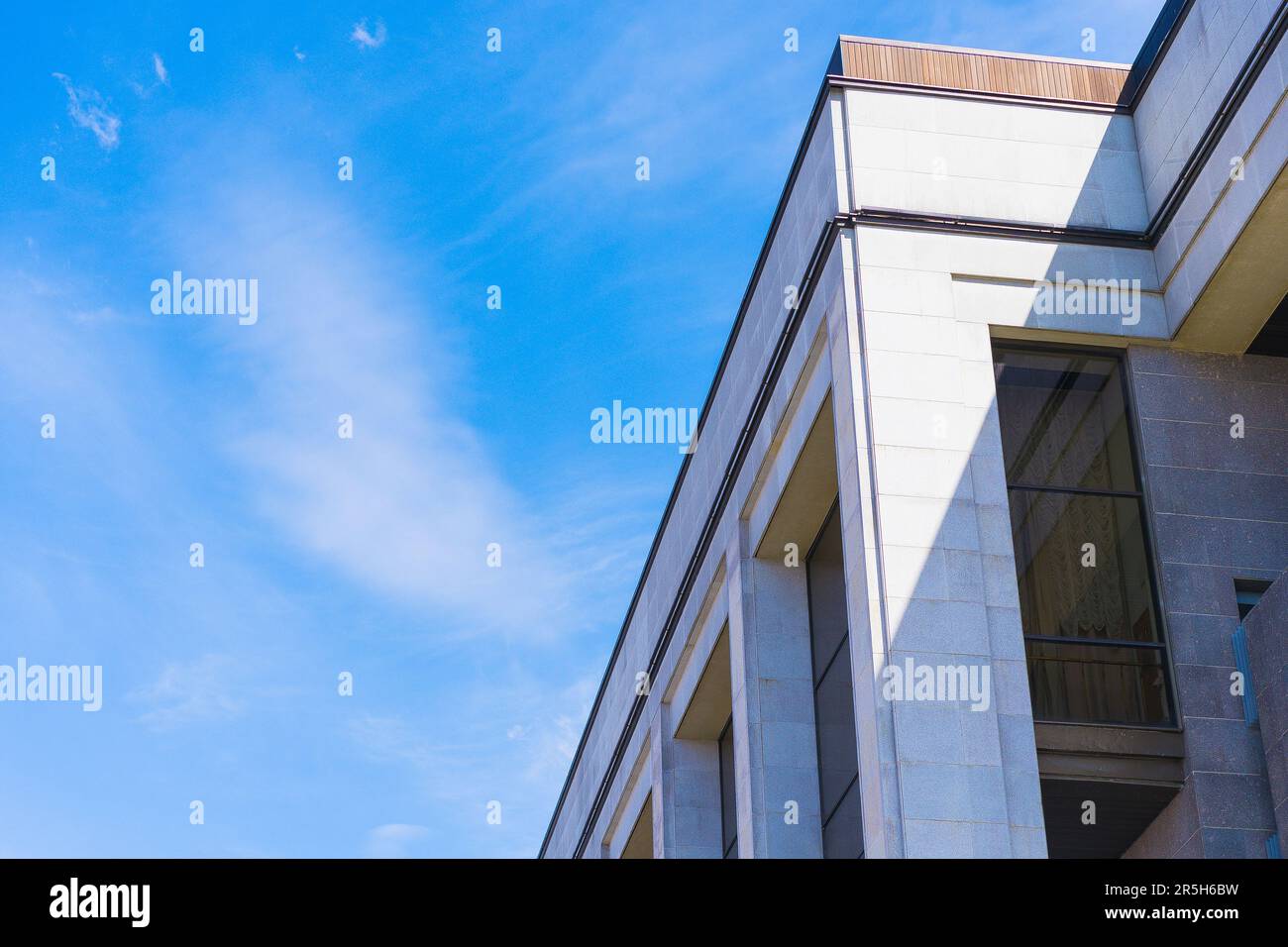 Gray granite clad building with large glass windows reflecting blue sky ...