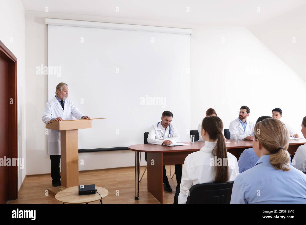 Senior doctor giving lecture in conference room with projection screen ...