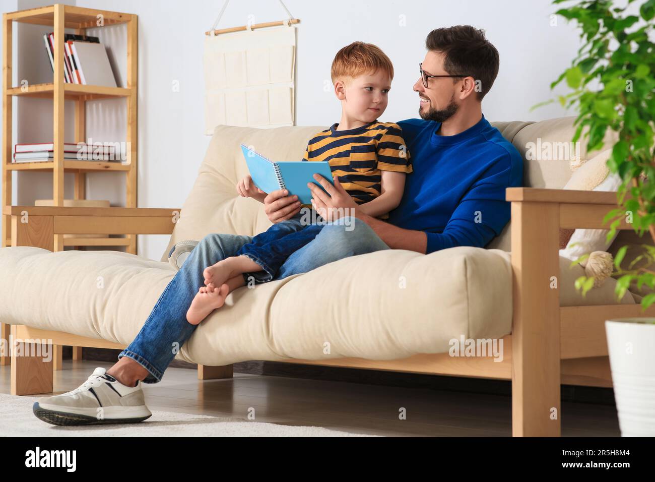 Father reading book with his son on sofa in living room at home Stock ...