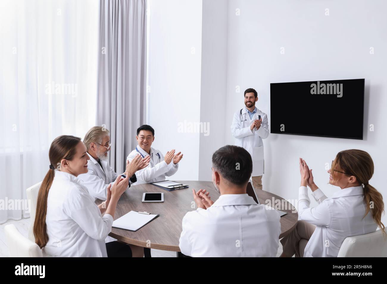 Team of doctors listening to speaker report near tv screen in meeting ...