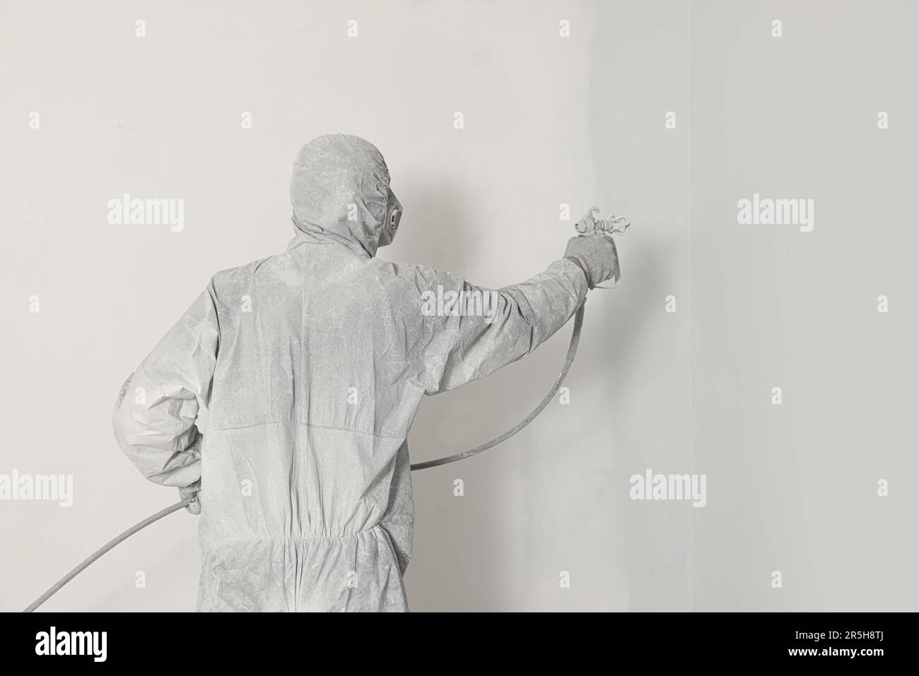 Decorator in uniform painting wall with sprayer indoors, back view ...