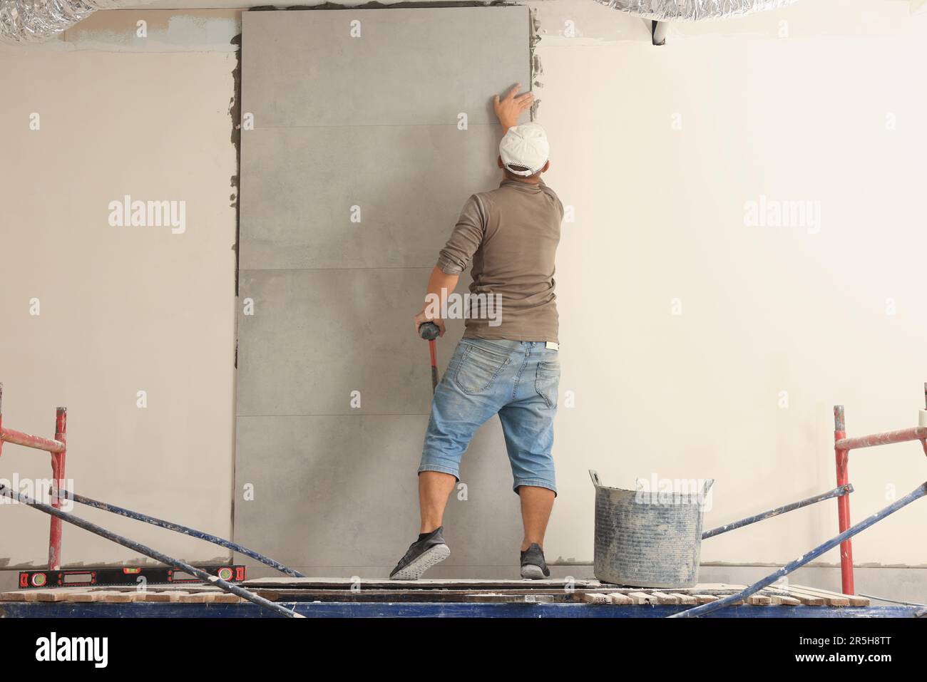 Worker installing tile on wall indoors, back view Stock Photo - Alamy