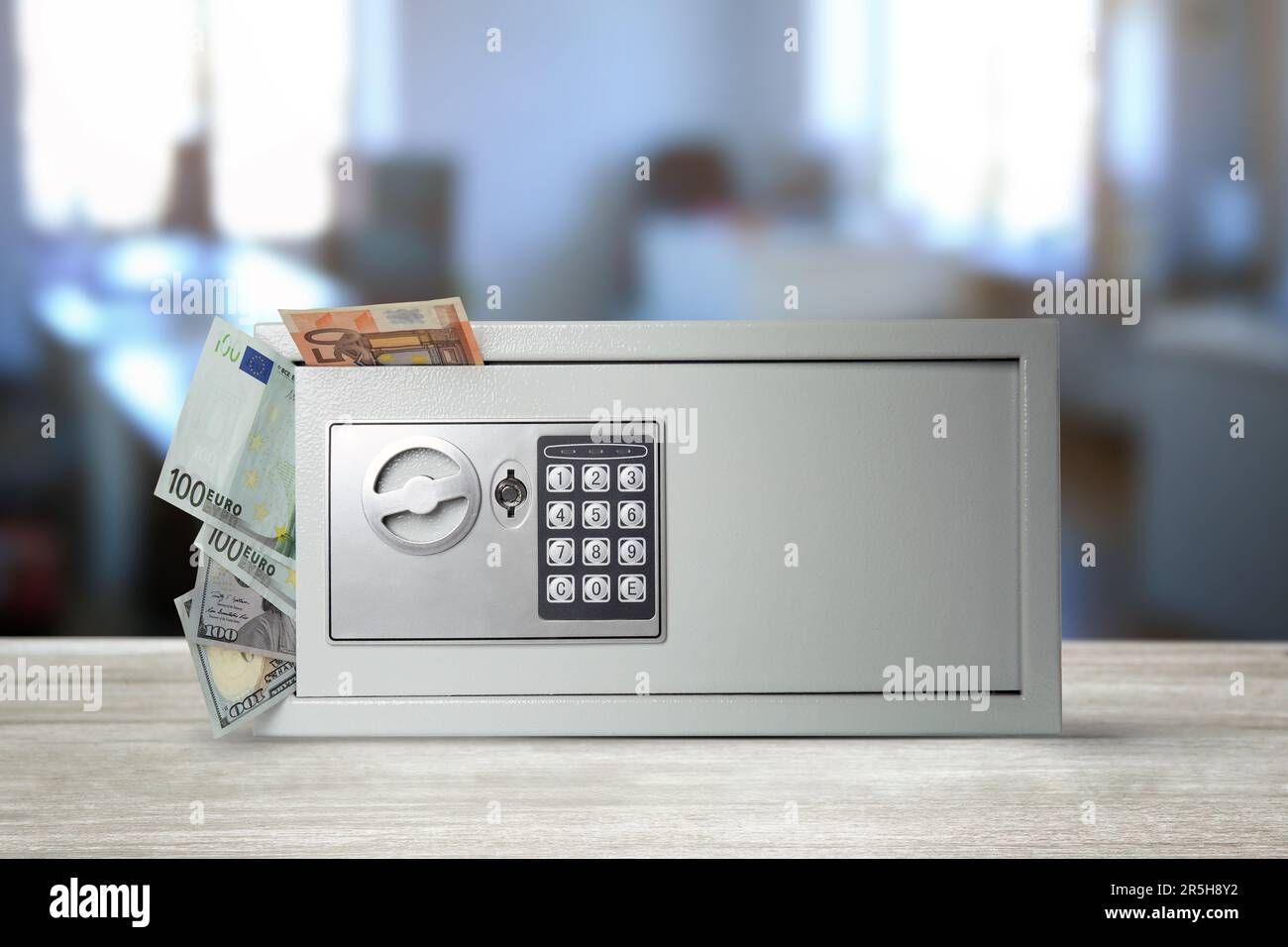 Closed steel safe with electronic lock and money on white wooden table ...