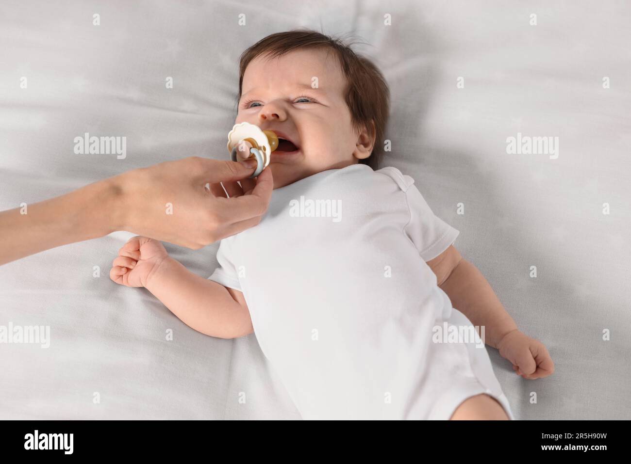 Mother giving pacifier to crying little baby on bed, closeup Stock ...
