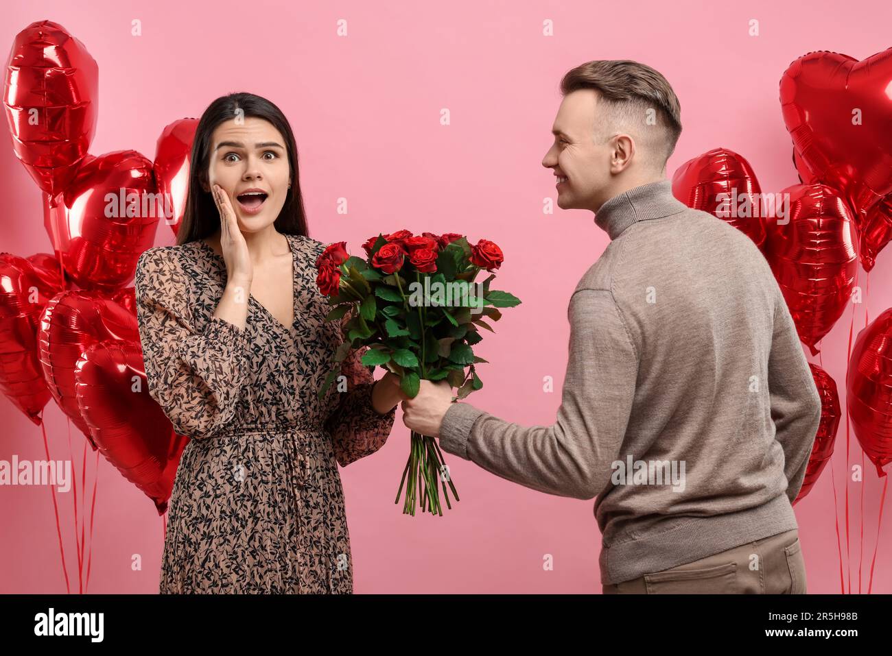 Boyfriend presenting bouquet of red roses to his girlfriend on pink ...