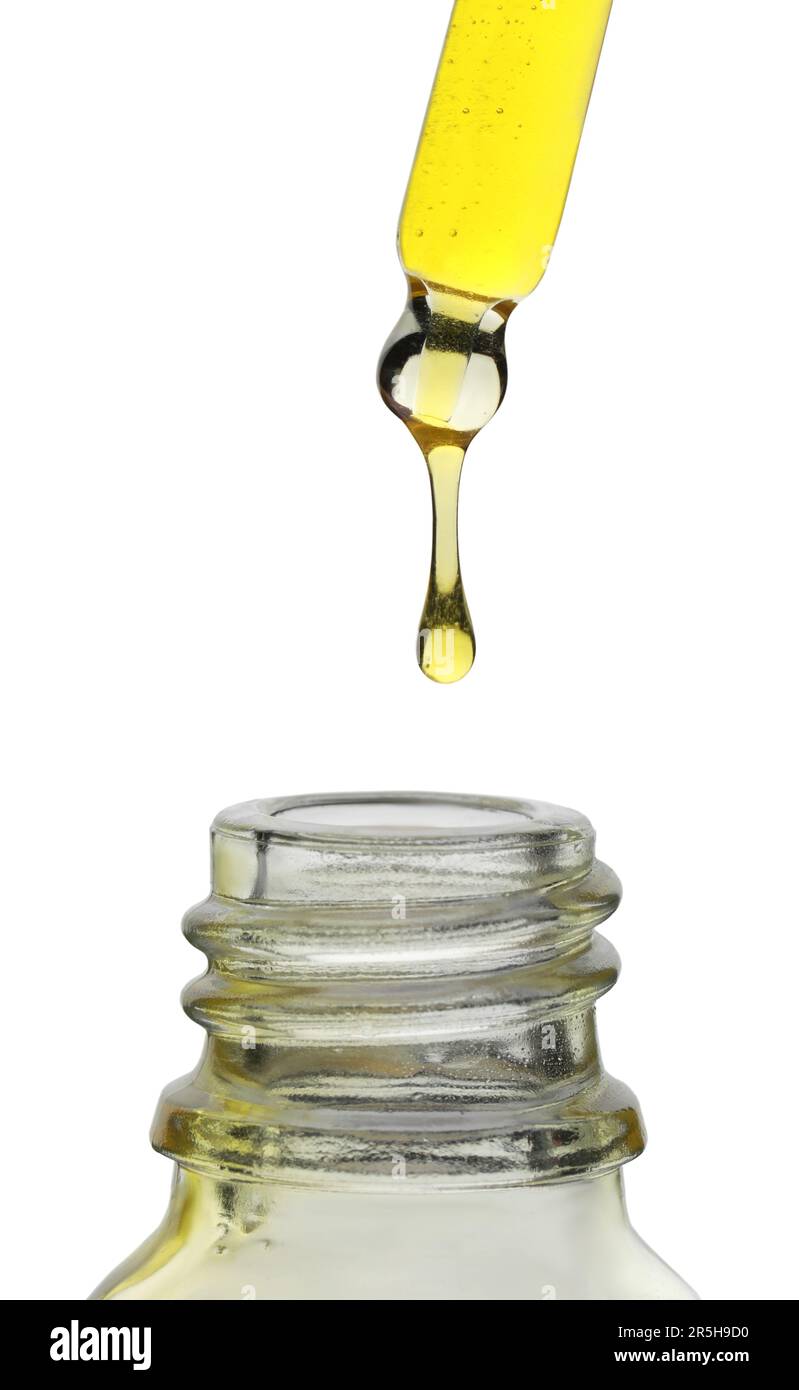 Dripping yellow facial serum from pipette into glass bottle on white ...