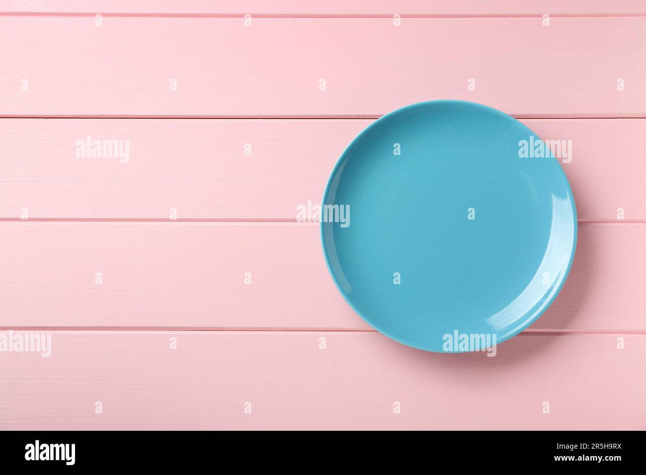 Clean light blue plate on pink wooden table, top view. Space for text ...