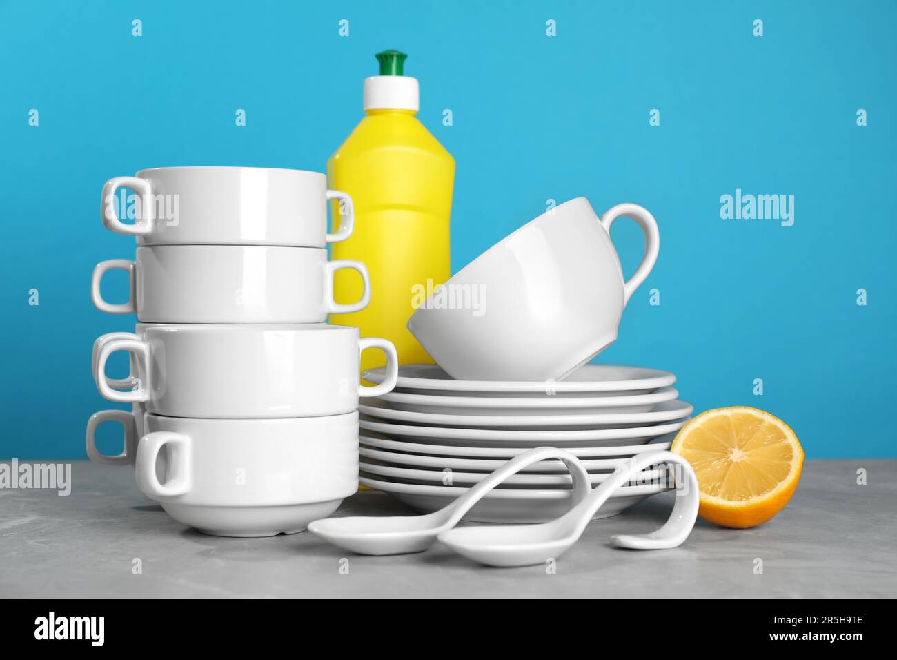 Clean tableware, dish detergent and lemon on grey table against light ...