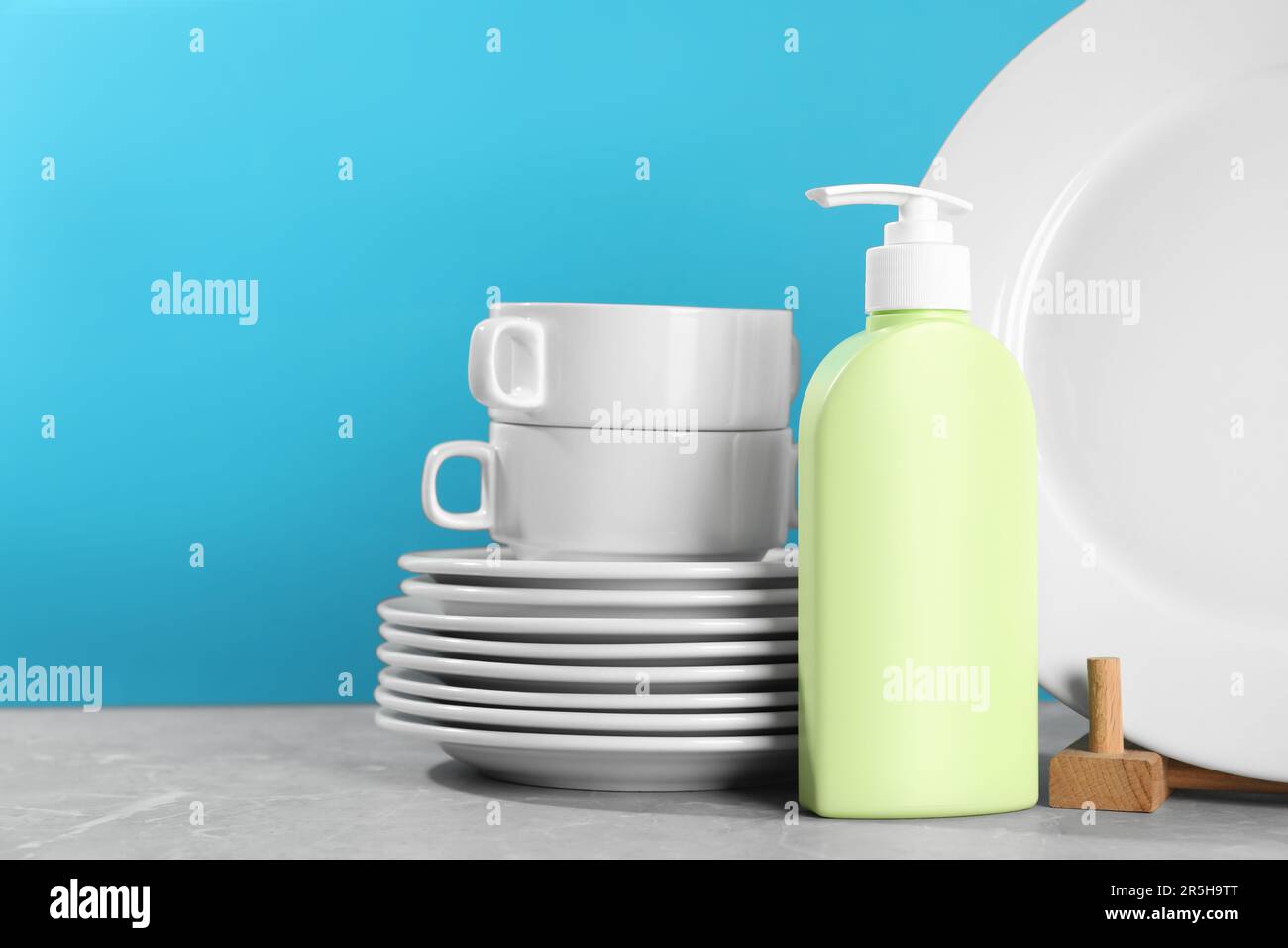Set of clean tableware and dish detergent on grey table against light ...