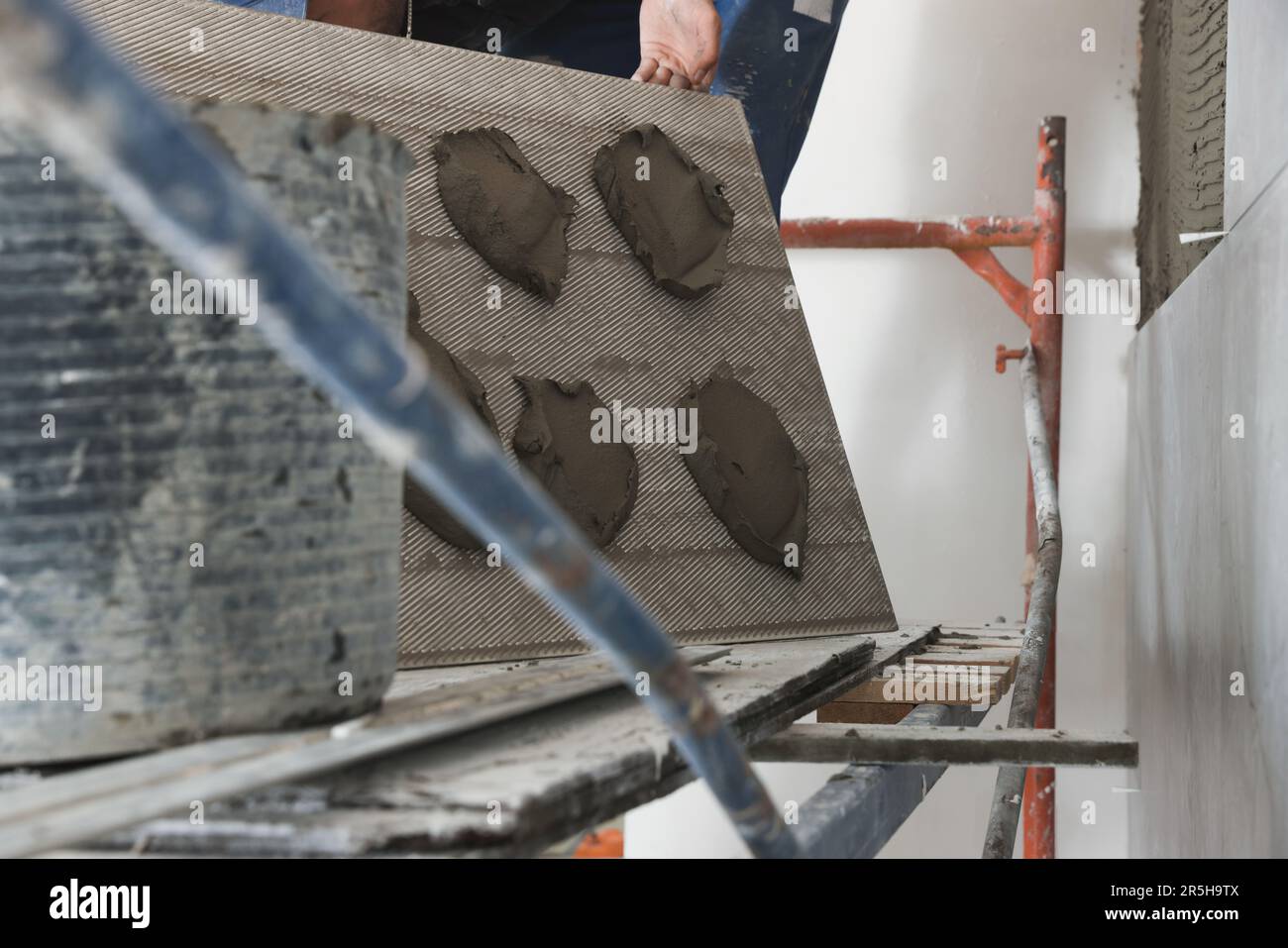 Worker applying cement on wall tile for installation indoors, closeup ...