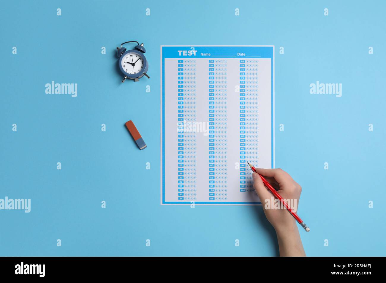 Student filling answer sheet on light blue background, top view ...