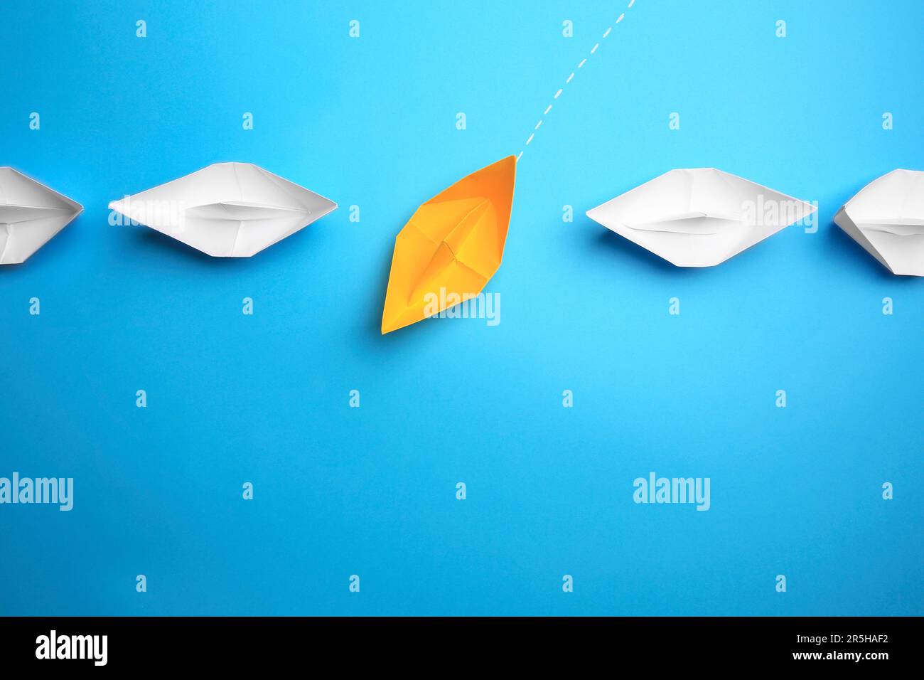 Yellow paper boat floating through others on light blue background ...