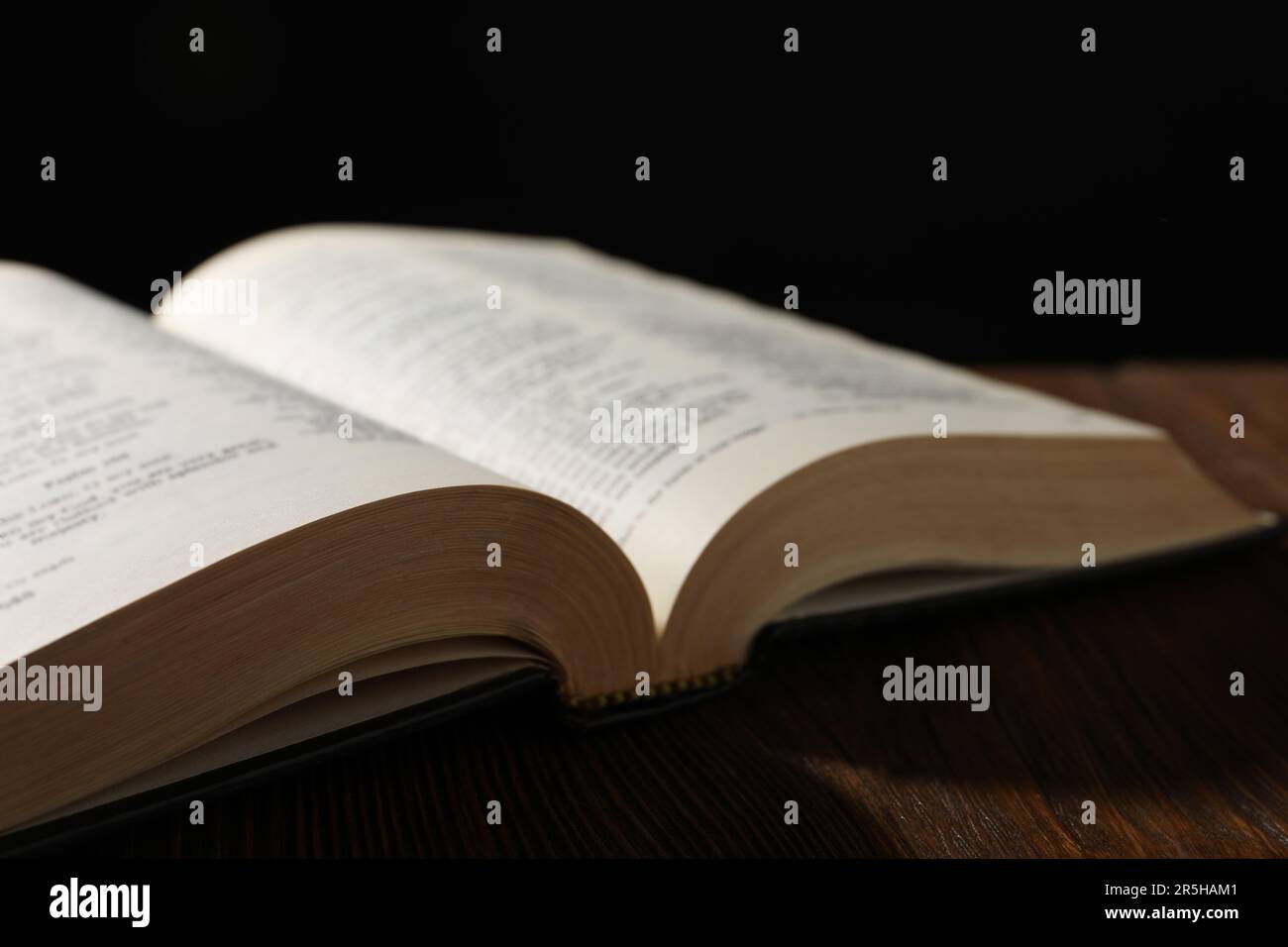 Open Bible on wooden table against black background, closeup Stock ...