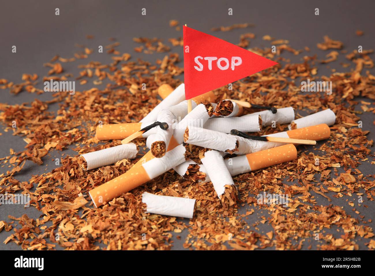 Flag with word Stop, broken cigarettes and burnt matches on dark grey ...