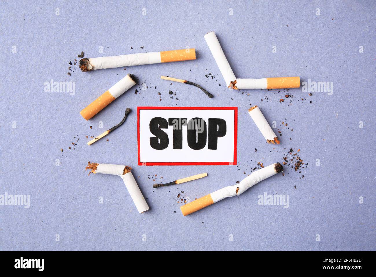 Card with word Stop, cigarette waste and burnt matches on light blue ...