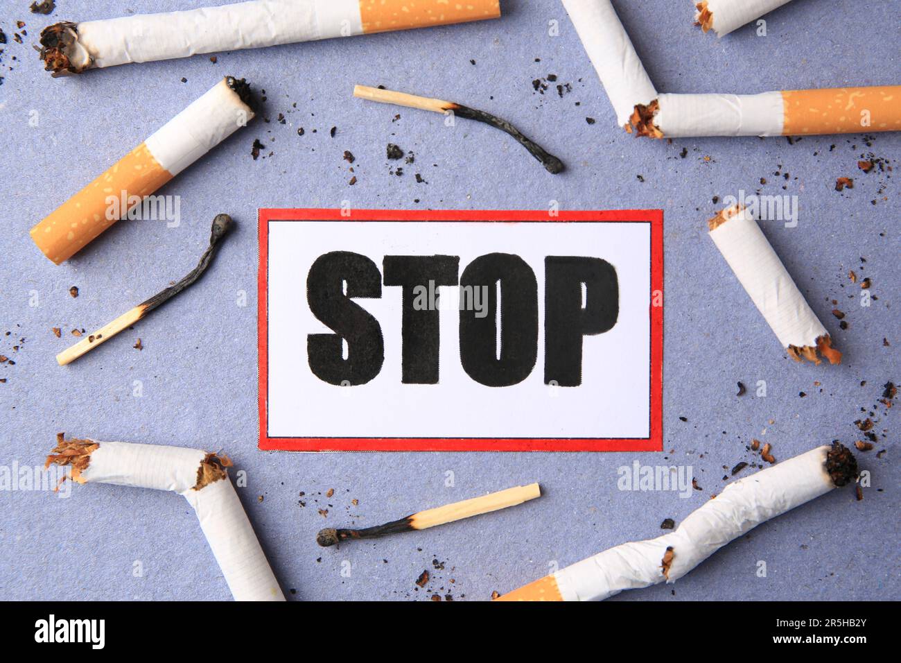 Card with word Stop, cigarette waste and burnt matches on light blue ...