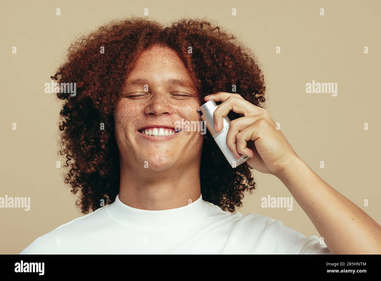 Happy young man applying face serum in a studio, pampering his skin to ...