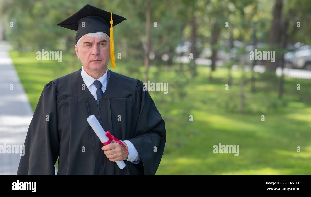Serious old man in graduation gown holding diploma outdoors Stock Photo ...