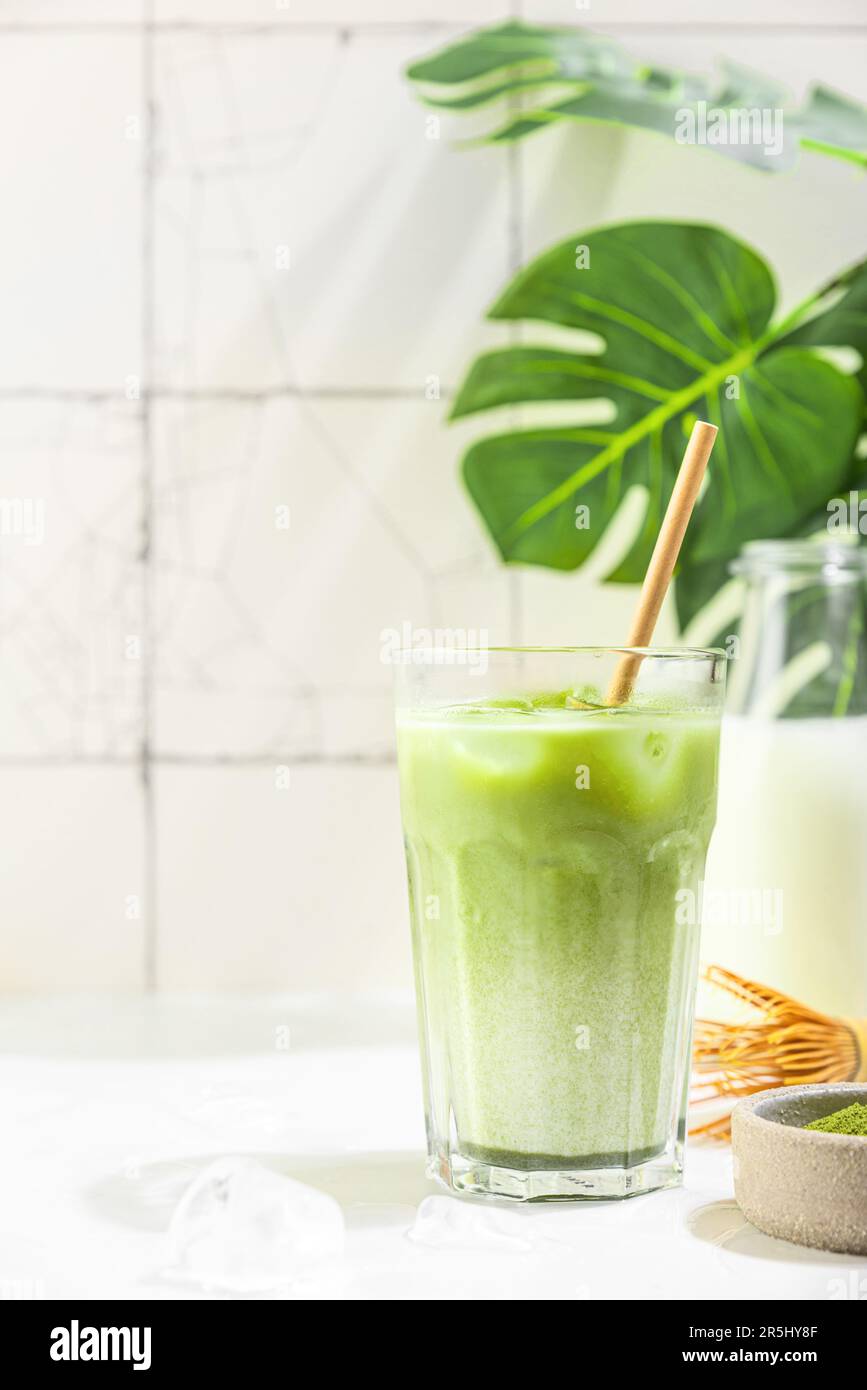 Iced green matcha latte in a glass with milk bottle on white tile ...