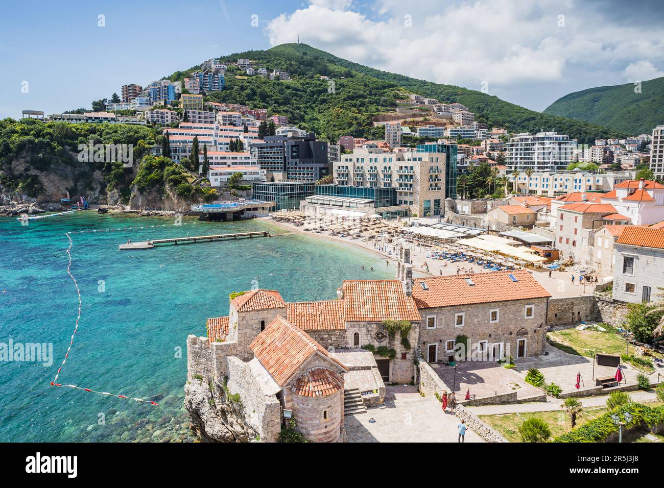 A small beach sat behind medieval buildings of the old town at Budva on ...