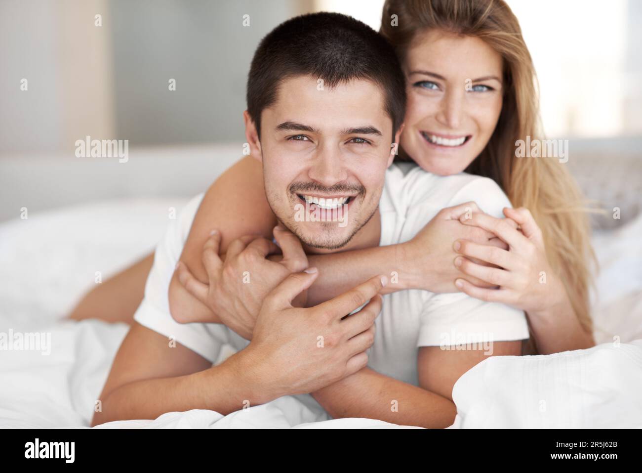 Sharing a special bond. Attractive young woman embracing her partner while they lie in bed ...