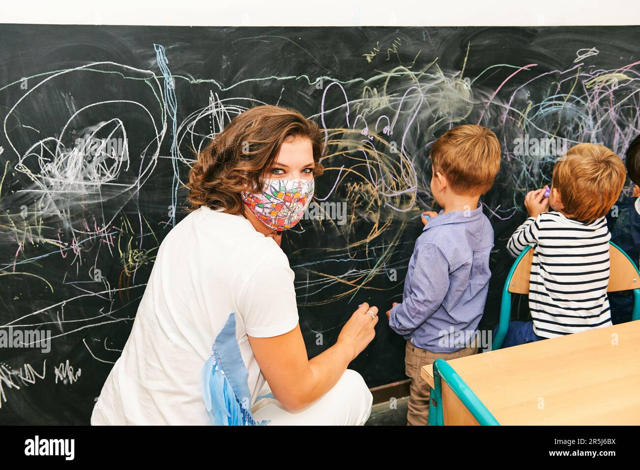 Art classroom in kindergarten, young teacher drawing with children on ...