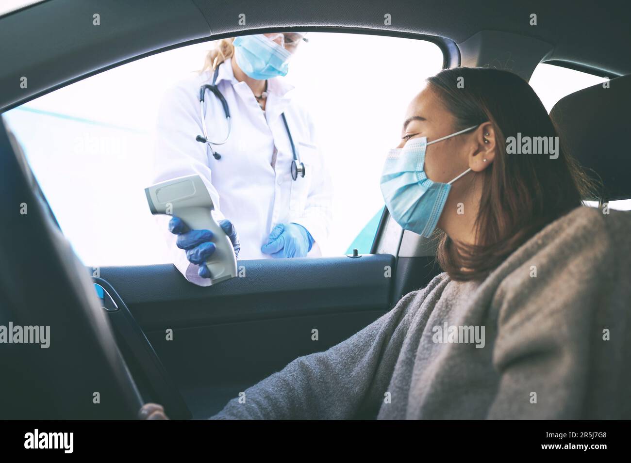 Get checked and get going. a masked young woman getting her temperature ...
