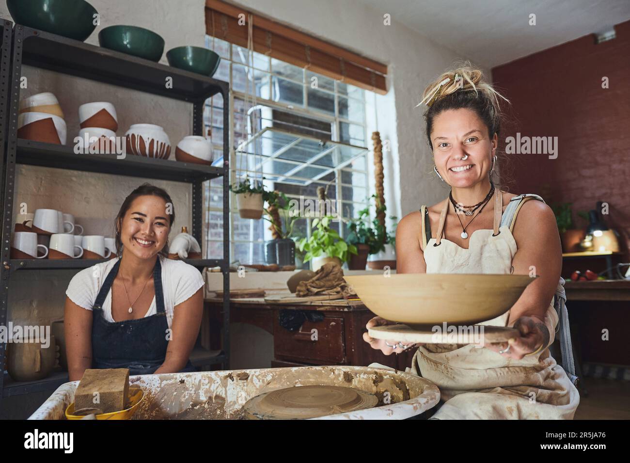 Just call us a couple of clay mates. two young women making a bowl in a ...