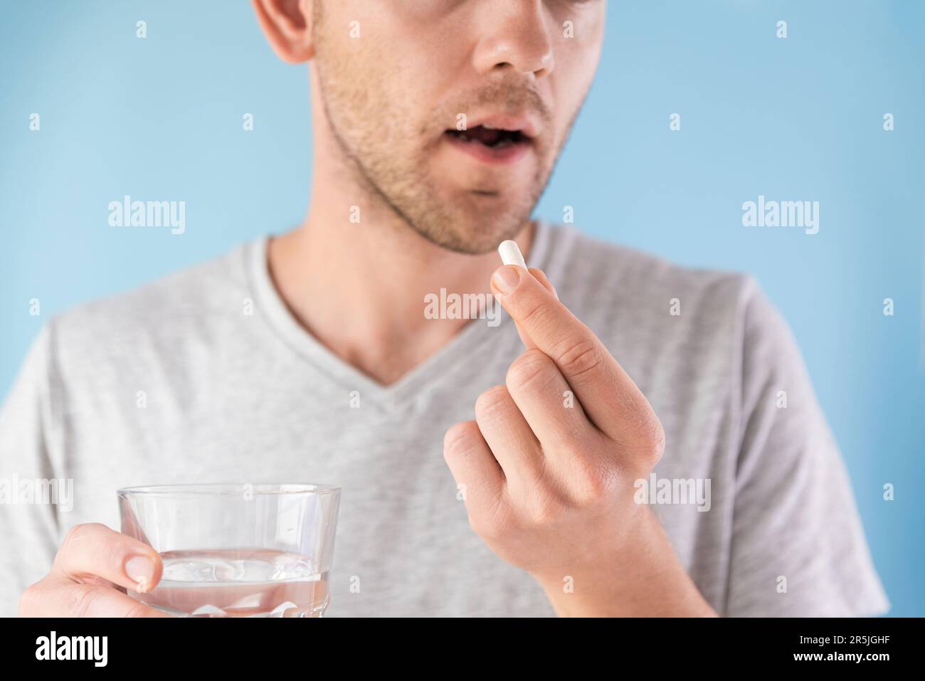 Man hold white capsule with collagen in male hand on blue background. Nutritional supplement ...