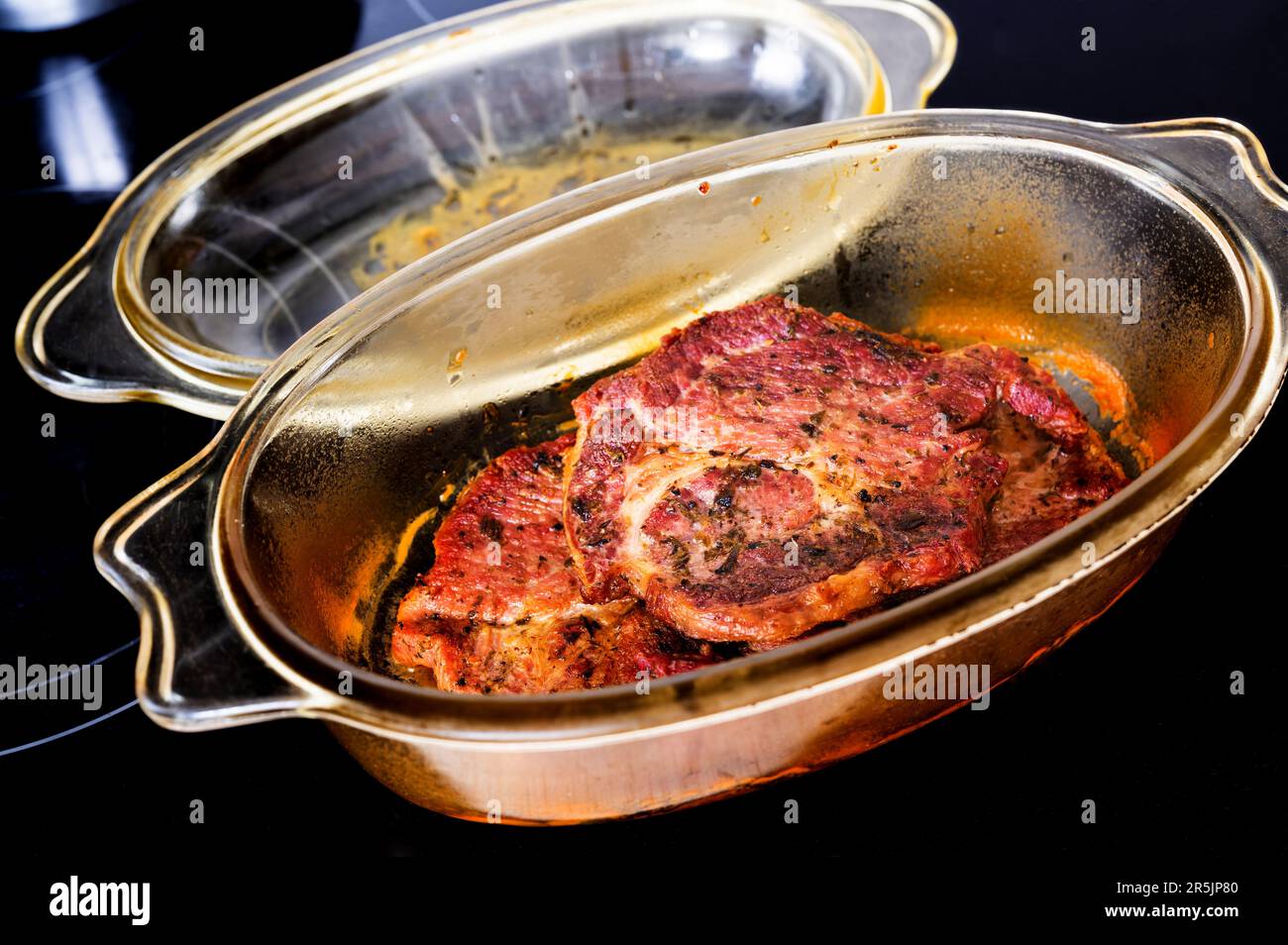Baked marinated spicy pork fillet in glass pan on black background of ...