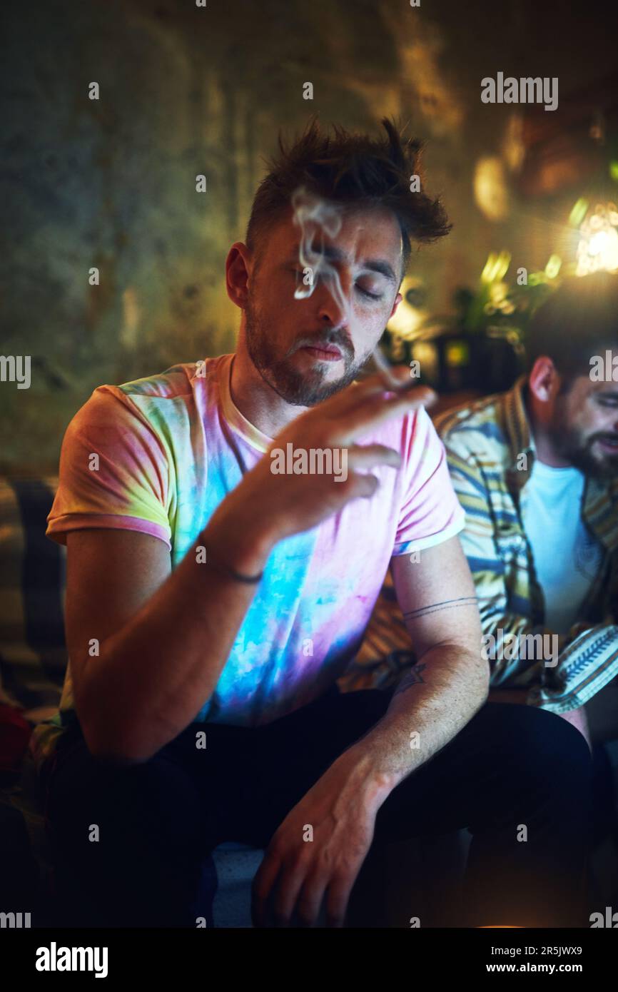 The smoke is doing its magic. a handsome young man smoking cannabis ...