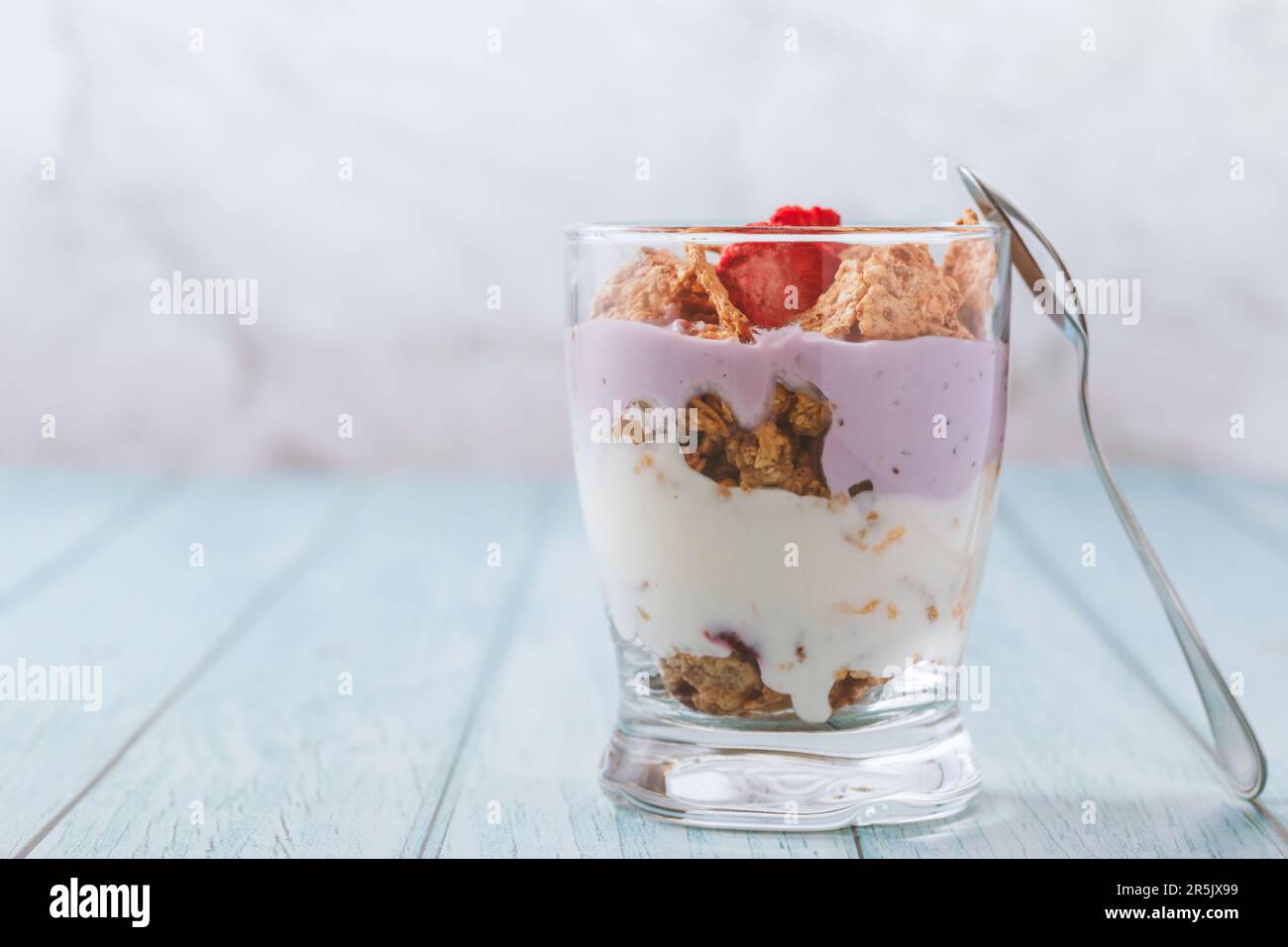 A glass tumbler with three layers of yogurt and muesli inside Stock ...