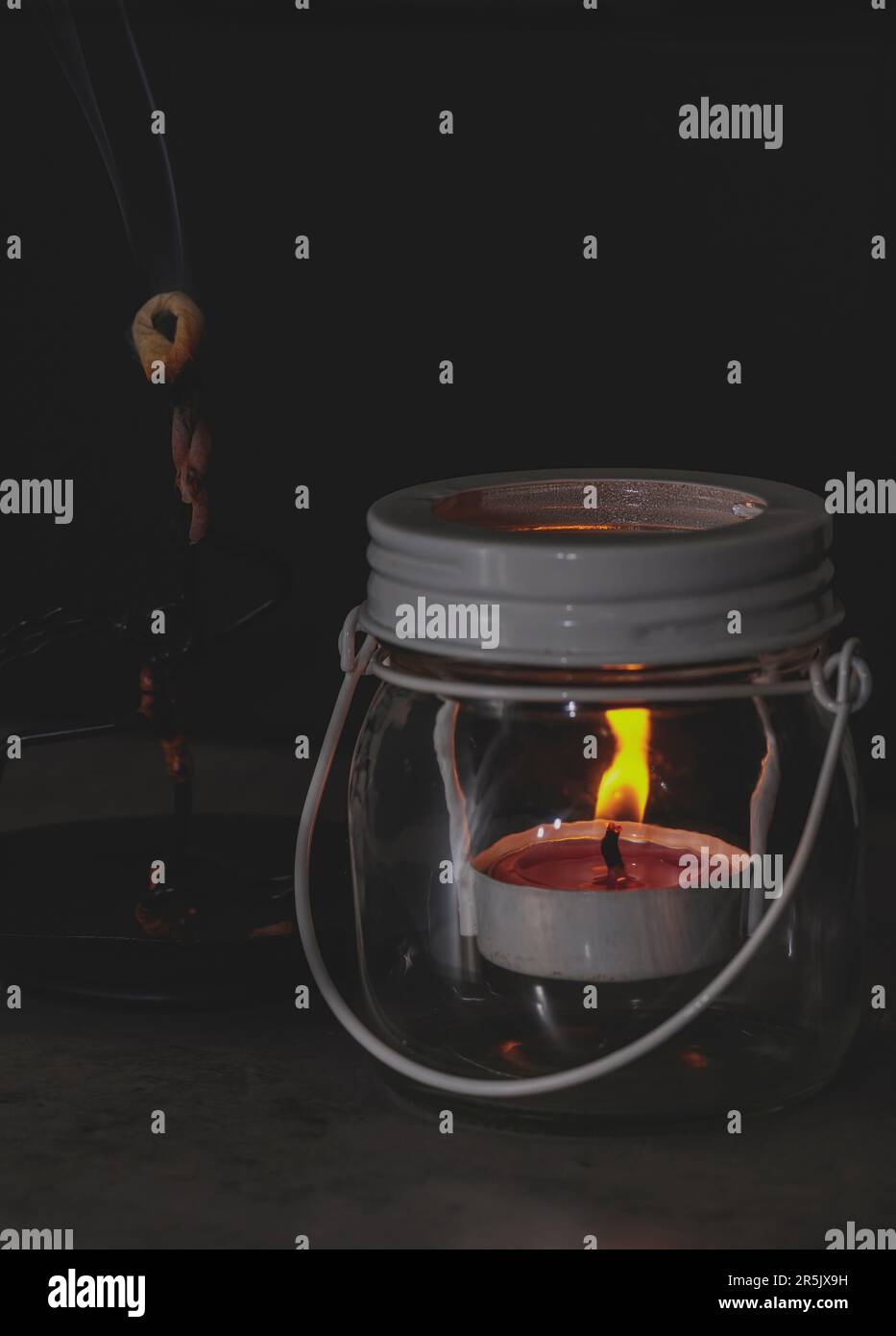 A small white lantern with a lighted candle inside. In the background ...