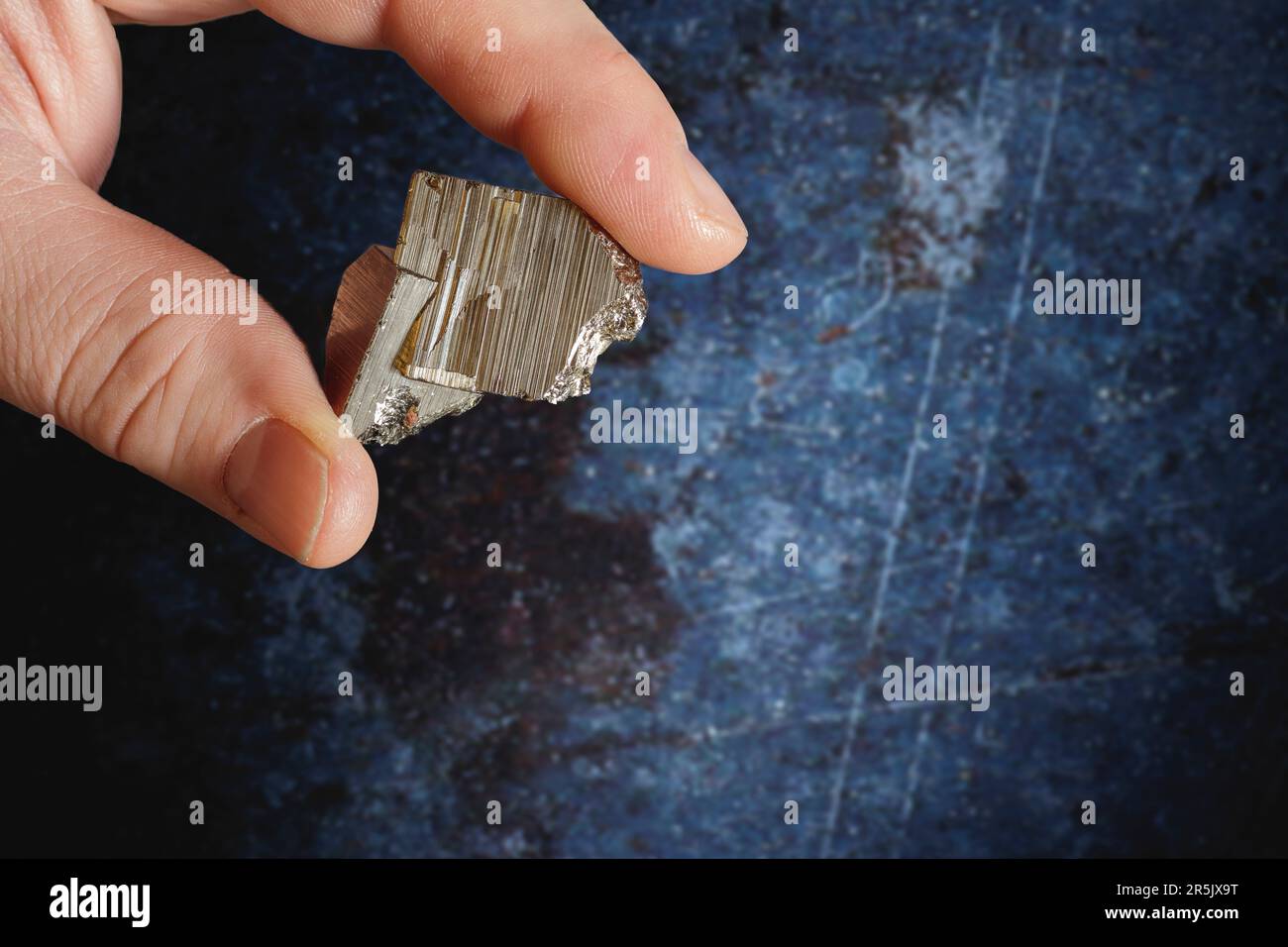 Caucasian man holding a pyrite mineral in his fingers on a rusty metal ...