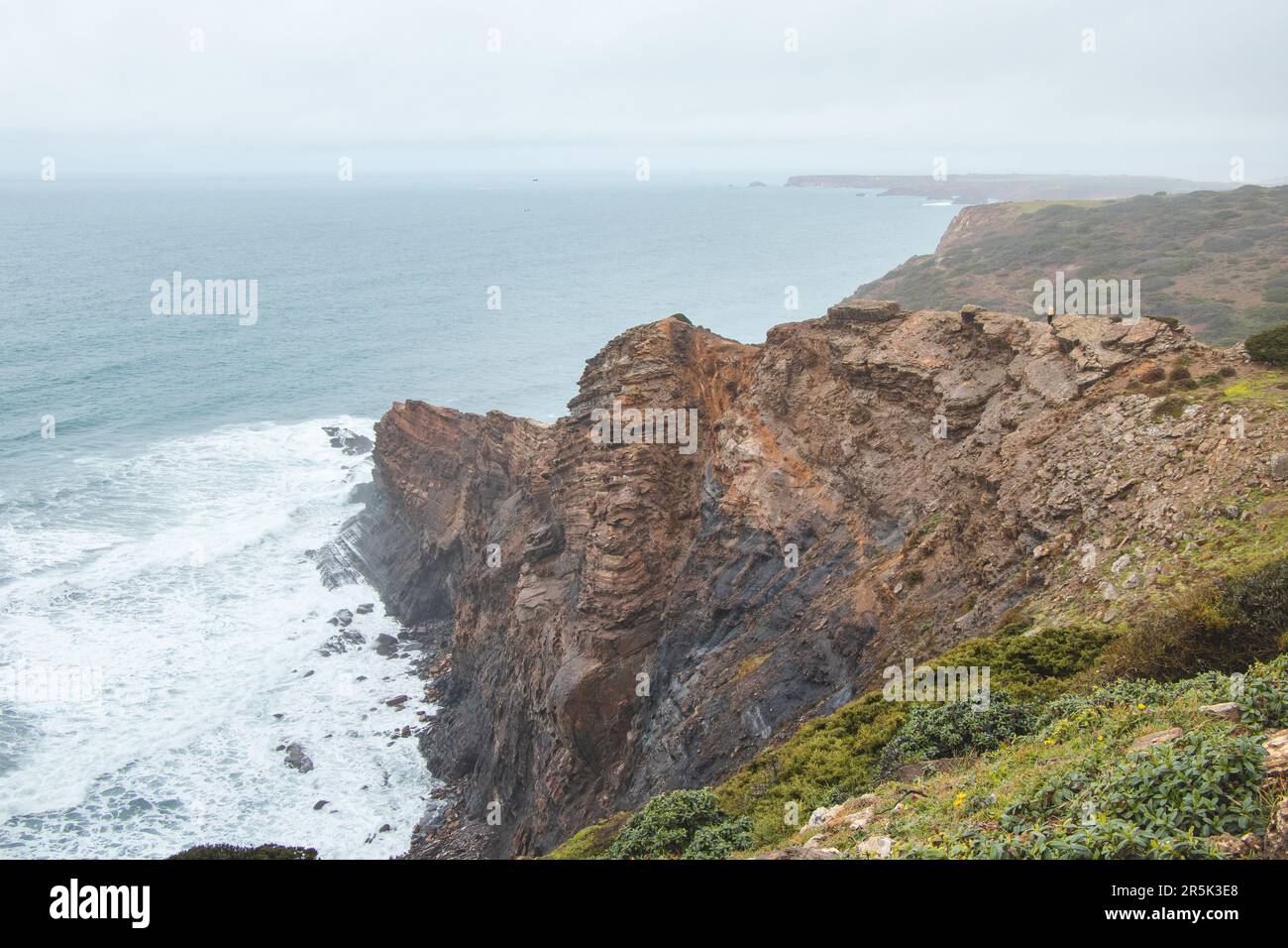 Adventurous man standing on the edge of a cliff enjoys the view of the ...