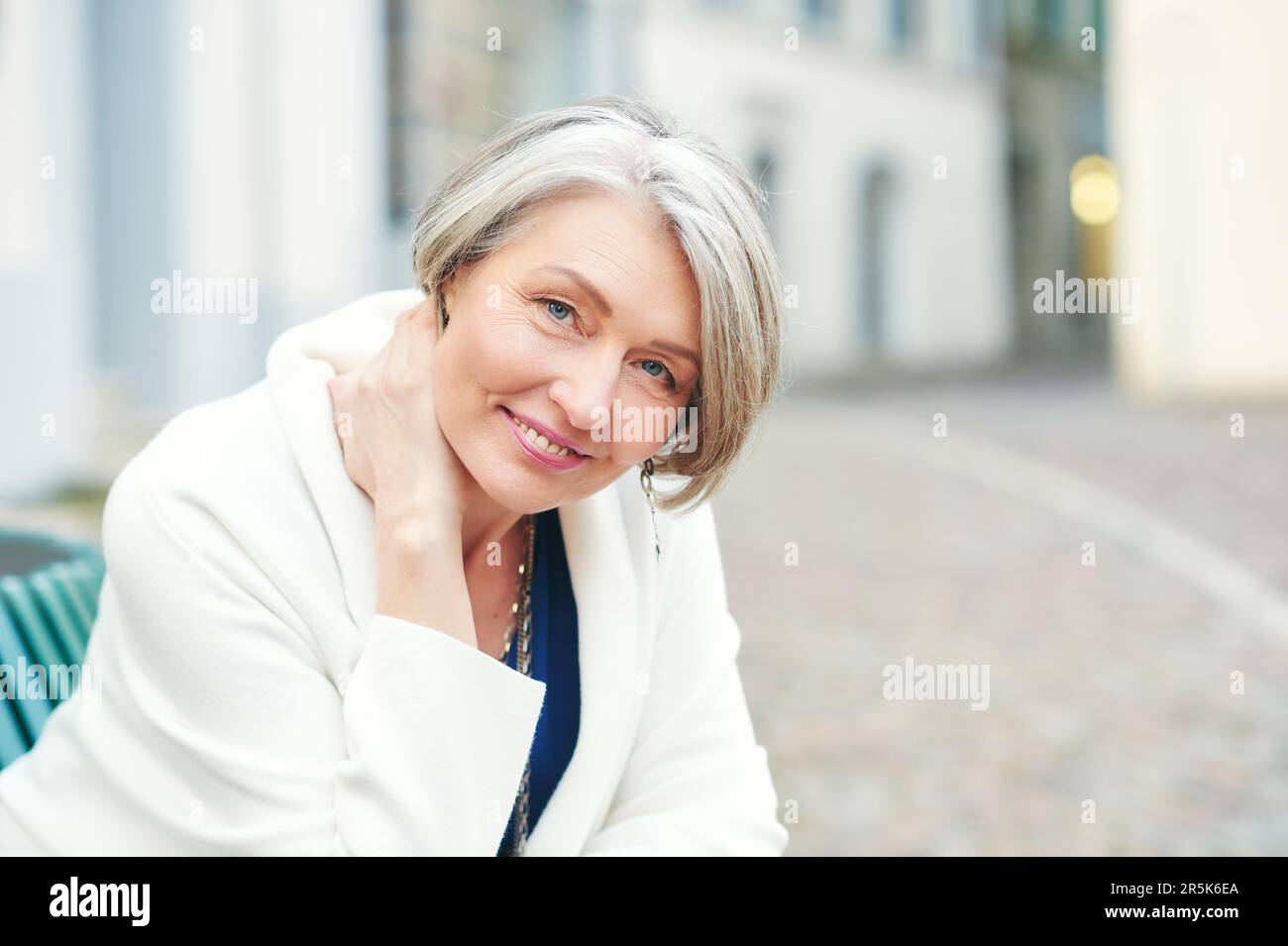 Outdoor portrait of beautiful and elegant middle age 55 - 60 year old woman, wearing white ...