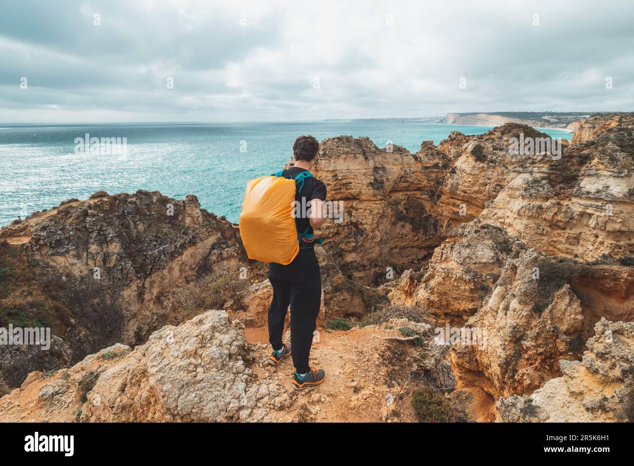 Adventurer with a backpack stands on the edge of a cliff and observes ...
