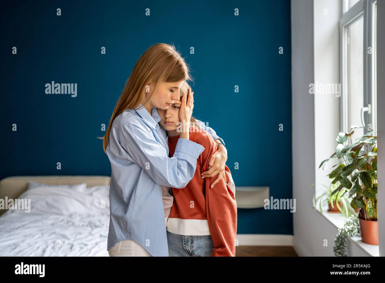 Young caring woman stands at home and hugging teenage girl needing ...
