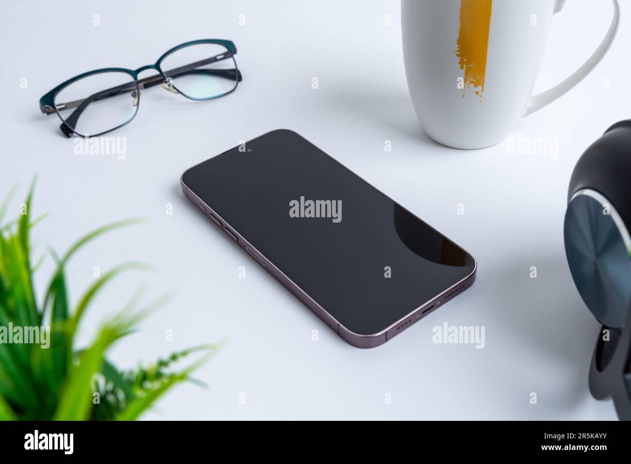 Phone placed beside office items like a headset, plant, glasses, and a ...