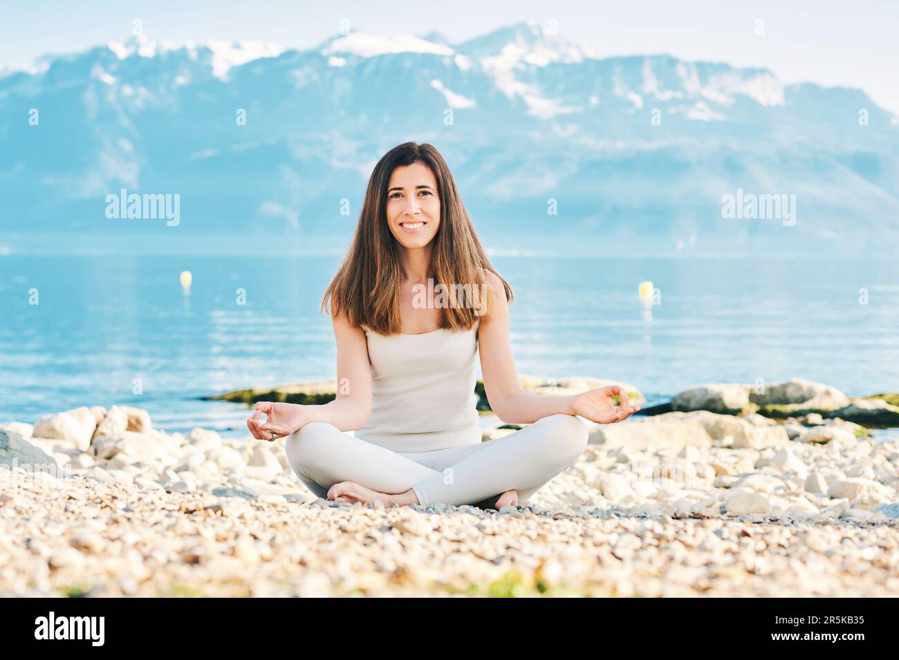 Beautiful spiritual woman meditating by the lake, wearing beige clothes ...