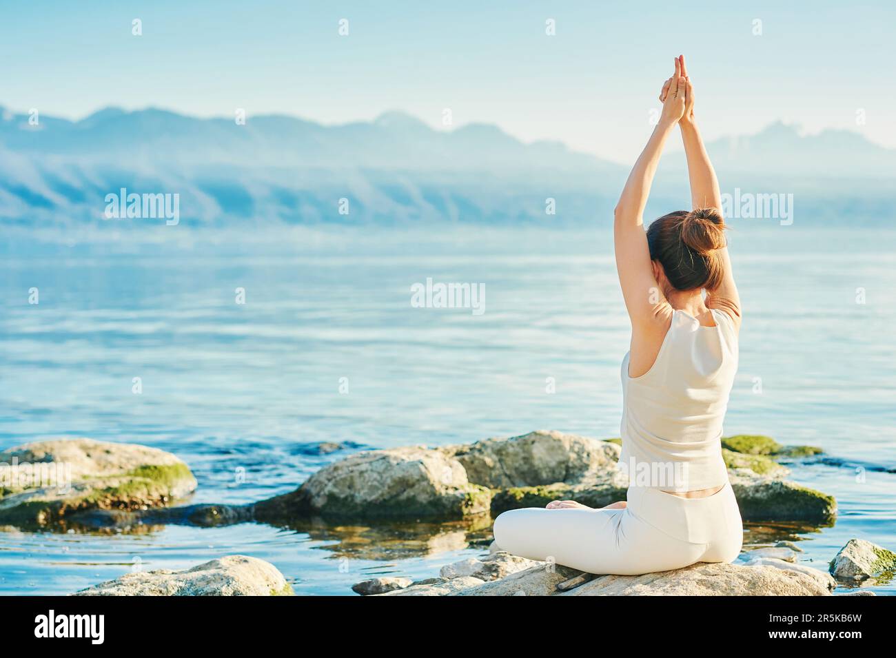 Beautiful spiritual woman meditating by the lake, wearing beige clothes ...