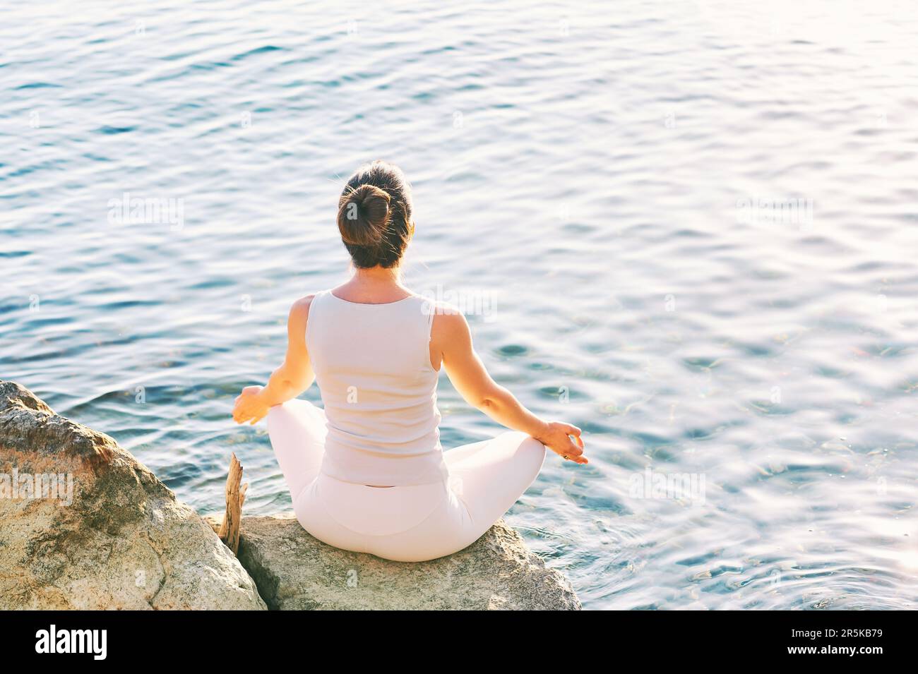 Beautiful spiritual woman meditating by the lake, wearing beige clothes ...
