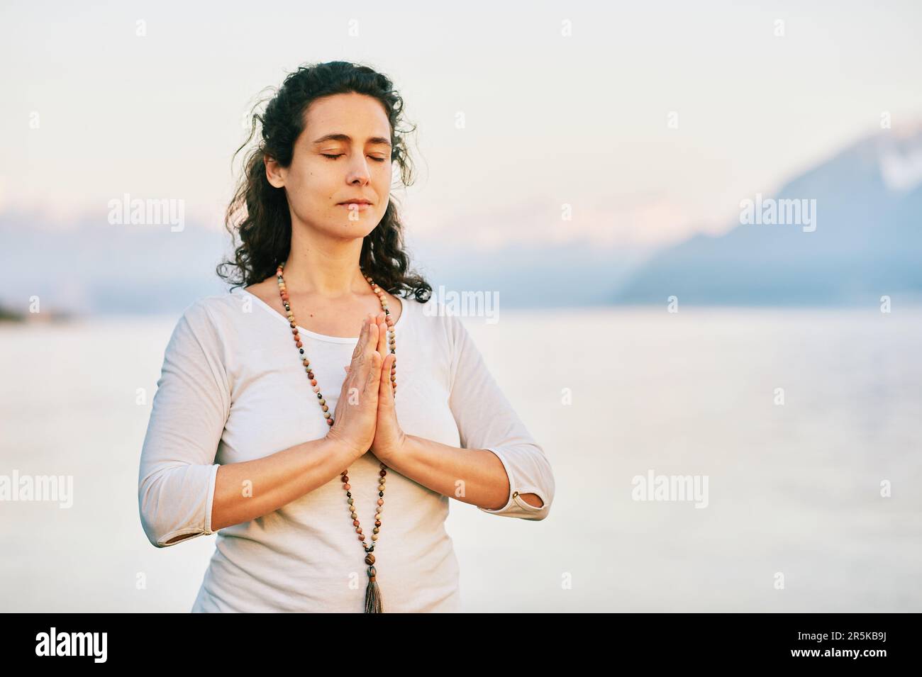 Beautiful spiritual woman meditating by the lake, wearing white clothes ...