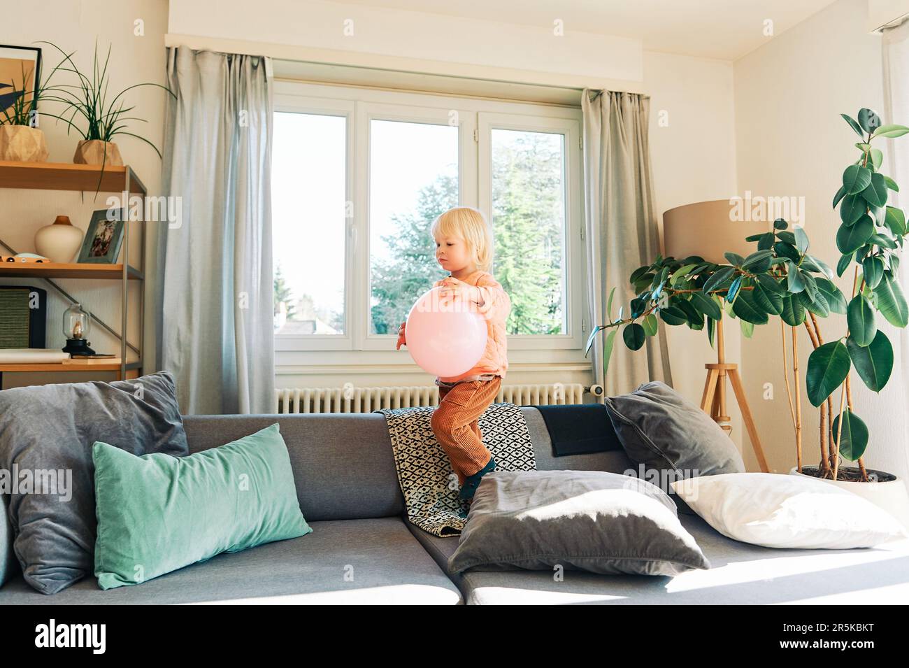 Cute little kid playing with baloon at home, walking on couch Stock ...