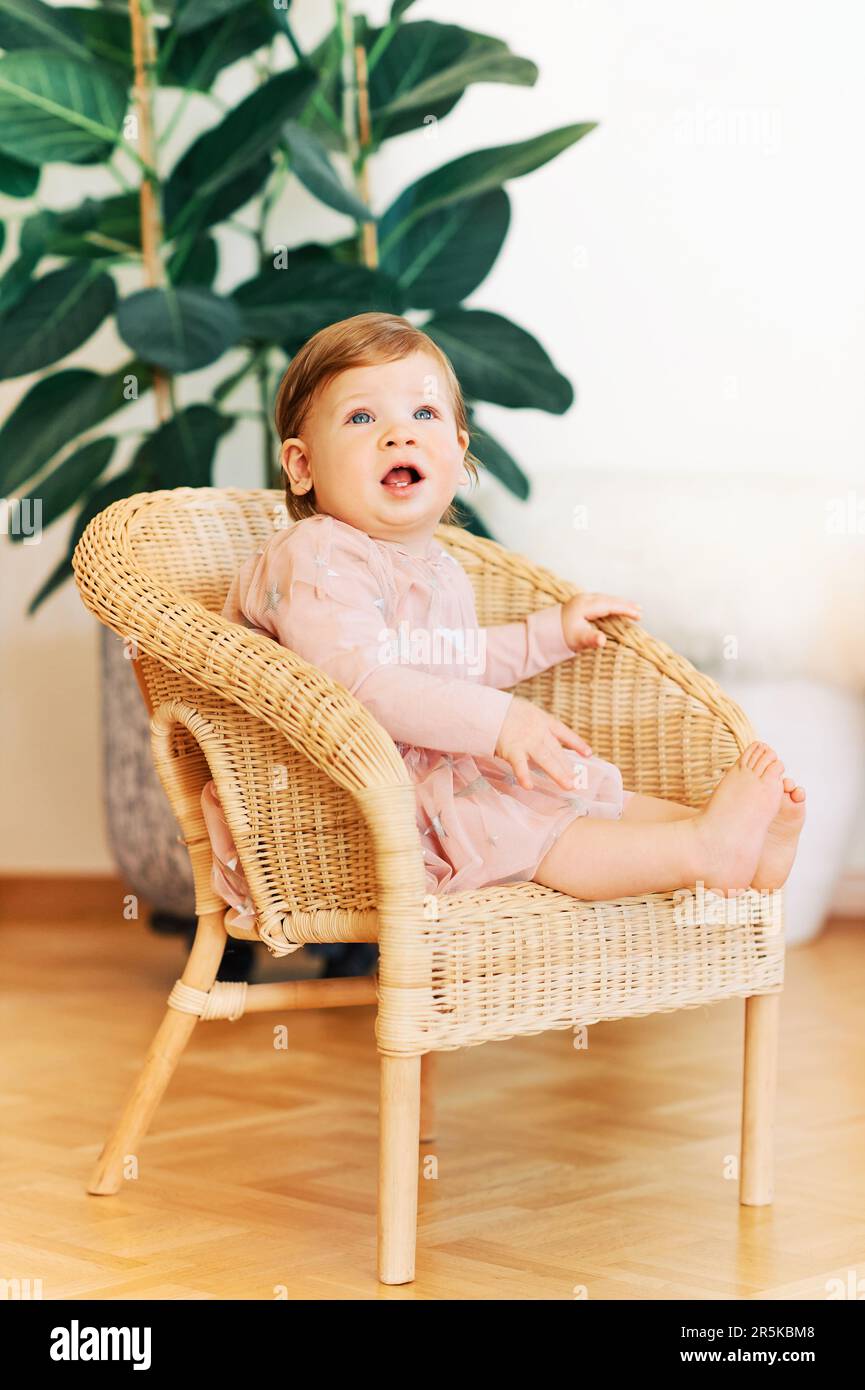 Interior portrait of adorable baby girl sitting on wicker chair ...