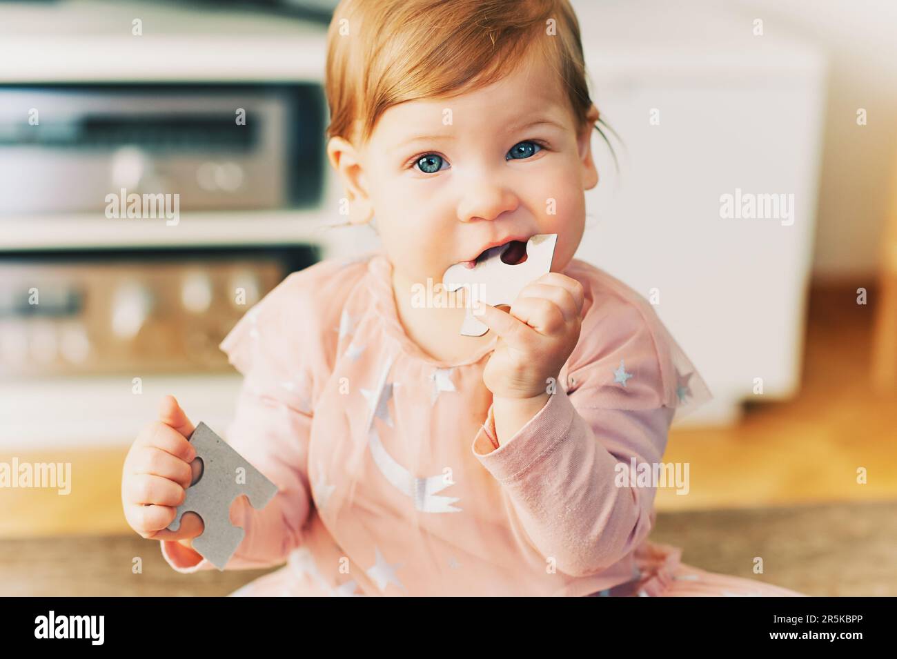 Funny toddler 1 year old girl holding puzzle pieces, chewing one part ...