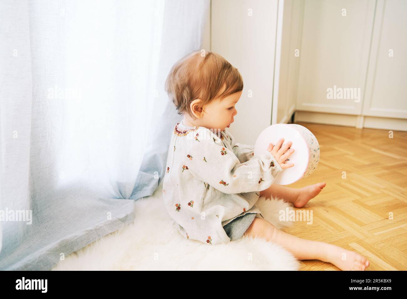 Interior portrait of adorable toddler girl sitting on the floor by the ...